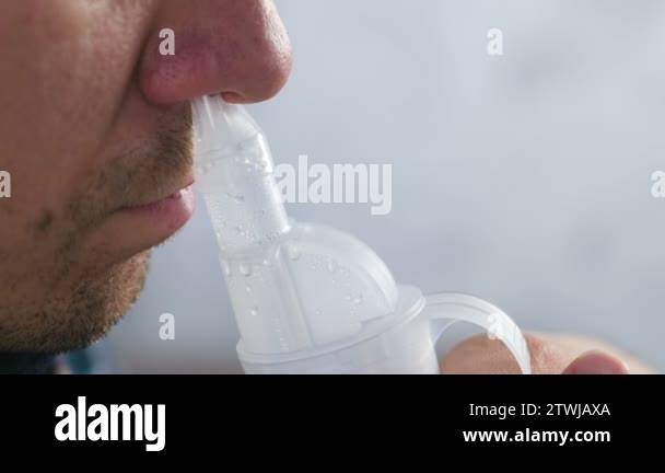 Sick man inhaling through inhaler nozzle for nose. Close-up nose, side ...