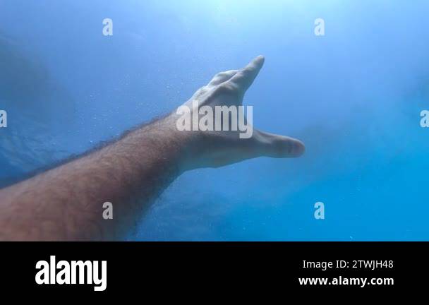 Male hand stretches from under the water to sunrays. Arm asking for ...