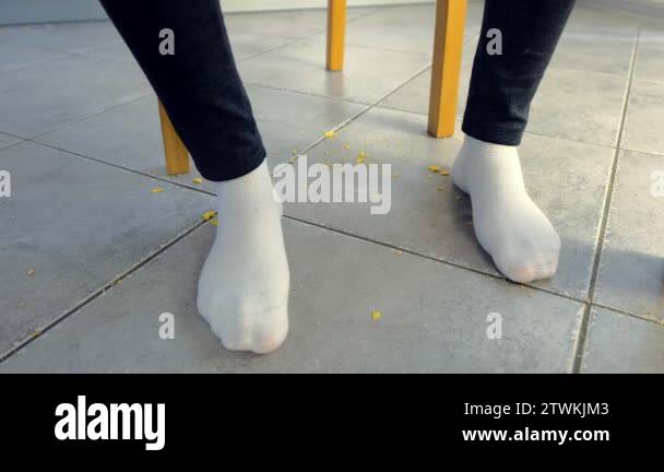 Woman eats at the table and crumbles corn flakes on the floor. Legs and ...
