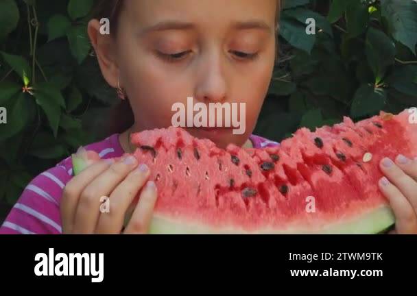 Teen girl eats a sweet, juicy watermelon on the background of greenery. The child enjoys a big ...