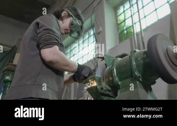 Woman blacksmith cutting a piece of metal from a screw using an angular grinding machine that ...