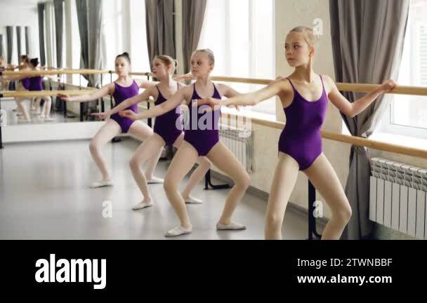 Small girls starting ballet-dancers in leotards are doing exercises ...