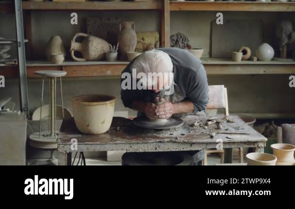 Creative senior potter is wetting hands in bowl with water and touching ...