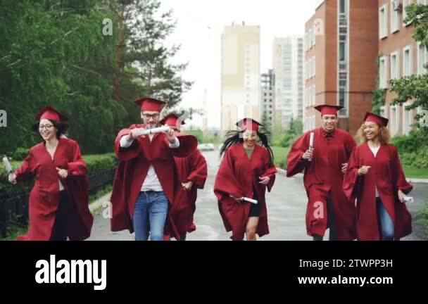 Excited graduating students running along road on campus holding ...
