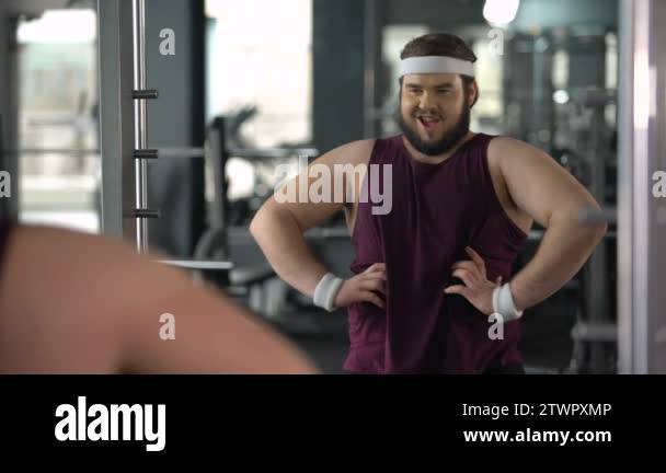 Funny fat man looking at mirror reflection gym and posing, pretending ...
