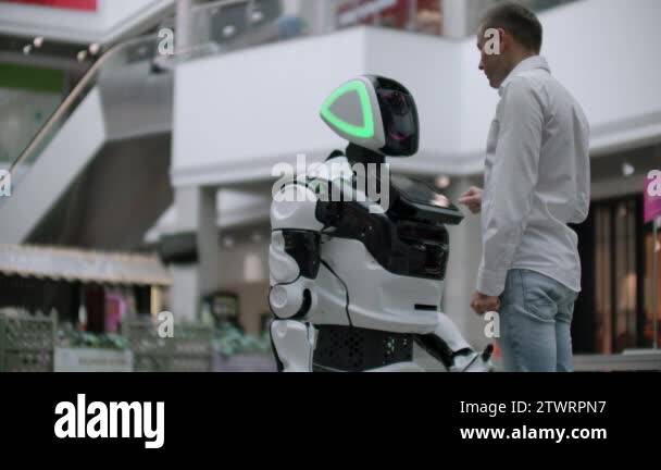 A man stands with a robot bot and asks him questions and asks for help ...