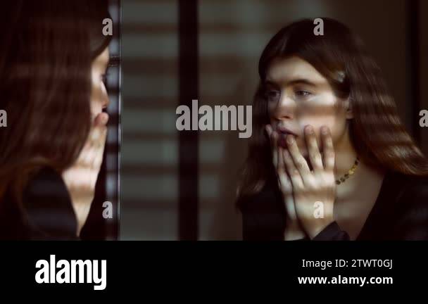 sad depressed woman looks herself in the mirror,touching her face in ...