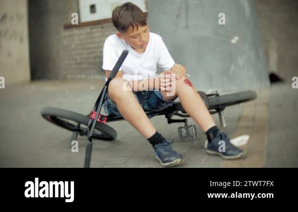 A young boy sits in a park after falling from a bike, calms the pain in ...