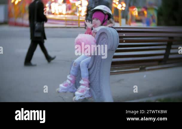 Beautiful little girl sitting on a bench in an amusement park, eating ...