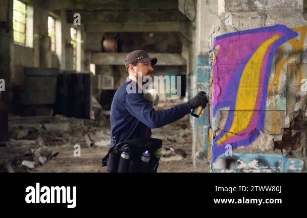 Young man professional graffiti painter is working inside abandoned ...
