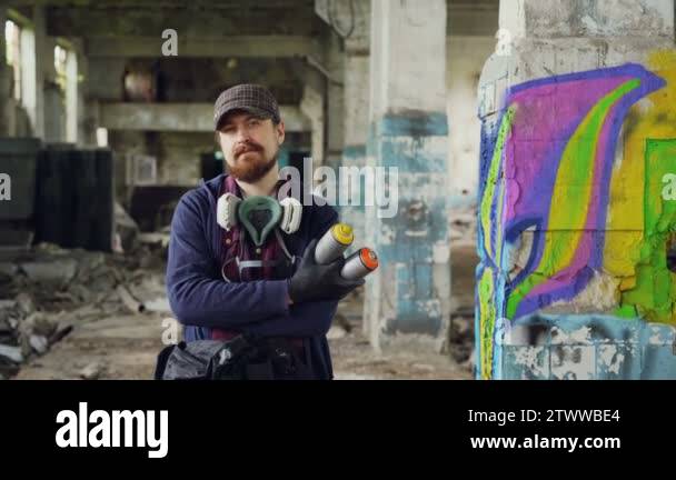 Portrait of bearded guy graffiti painter standing in old empty building ...