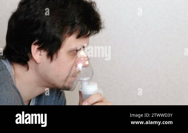 Use nebulizer and inhaler for the treatment. Young man inhaling through ...