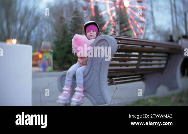 Beautiful little girl sitting on a bench in an amusement park, eating ...