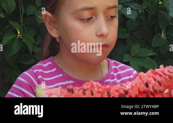 Teen girl eats a sweet, juicy watermelon on the background of greenery. The child enjoys a big ...