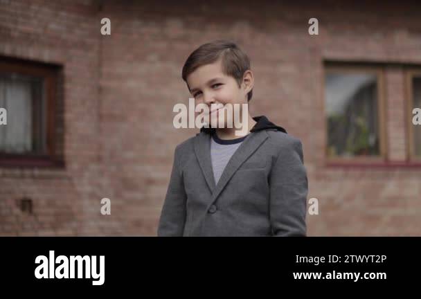Little boy with hairstyle in front of brick wall poses to camera and ...