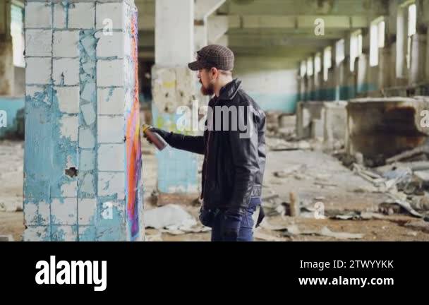 Side view of graffiti artist bearded guy drawing on damaged column ...