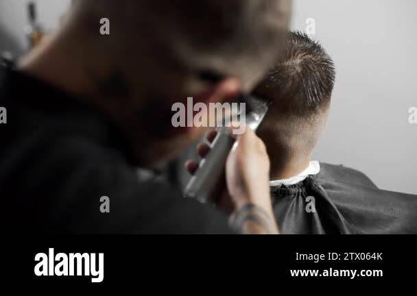 Tattoed barber makes haircut for customer at the barber shop by using ...