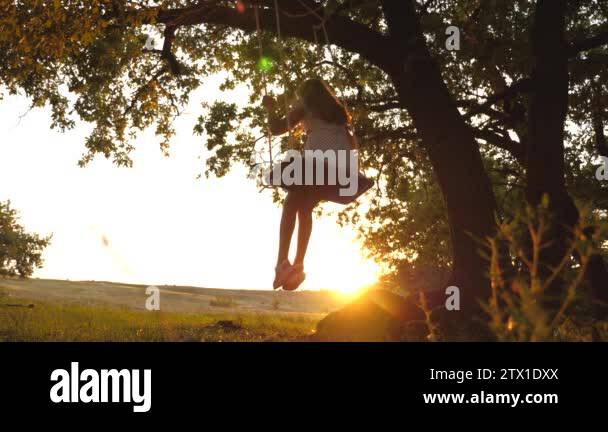 child rides a rope swing on an oak branch in forest. girl laughs ...