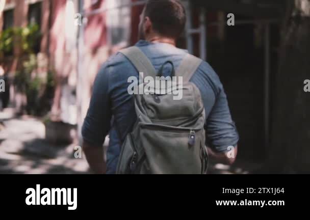 Camera follows young relaxed local man with backpack walking along ...
