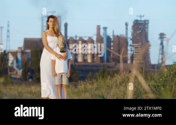 Mom and son in a gas mask stand in the background of a factory and ...