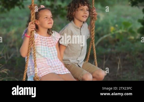 Couple of happy kids hugging and swinging on wooden swing at golden ...