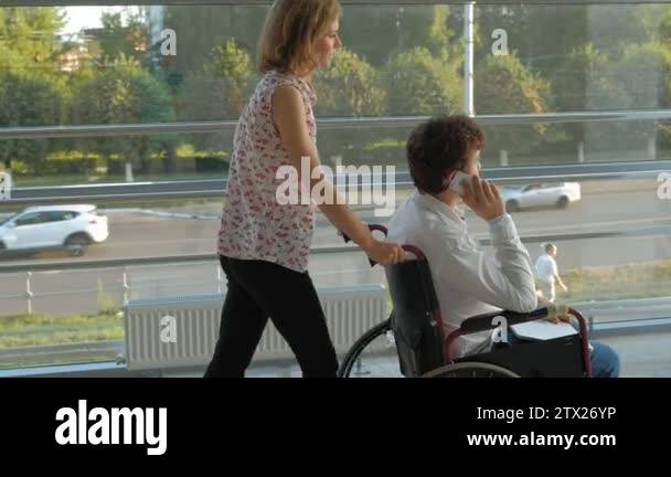 Business woman wheeling a wheelchair with a disabled businessman on a ...