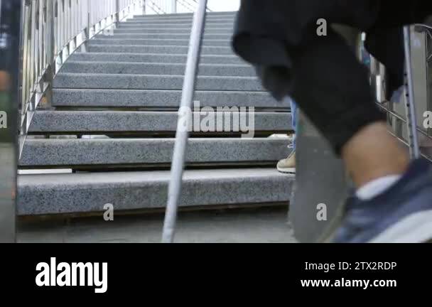 Young man with one leg on crutches with skateboard climbs the stairs ...