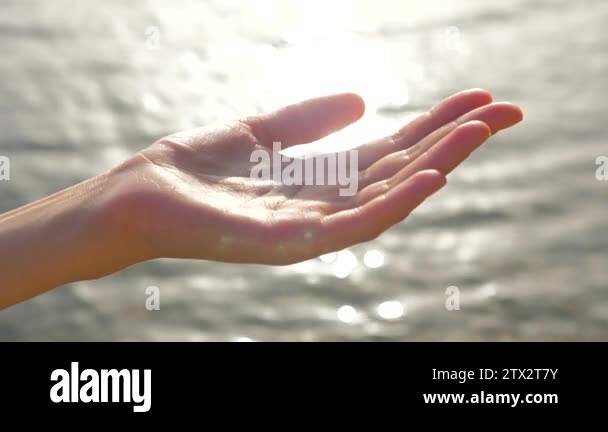 Female cupped hand catches falling water drops on seascape background ...