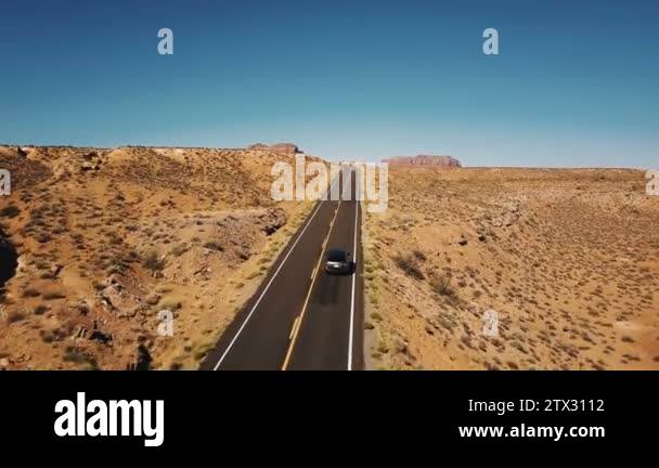Drone rising up above car moving along empty desert road to reveal ...