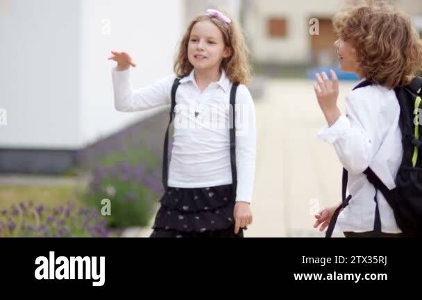 A pair of curly schoolchildren, a boy and a girl, say goodbye, waving ...