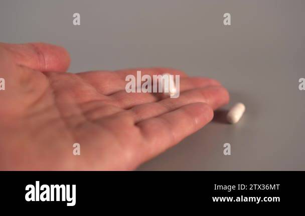 White medical capsules fall on the palm of a hand, bouncing and rolling ...