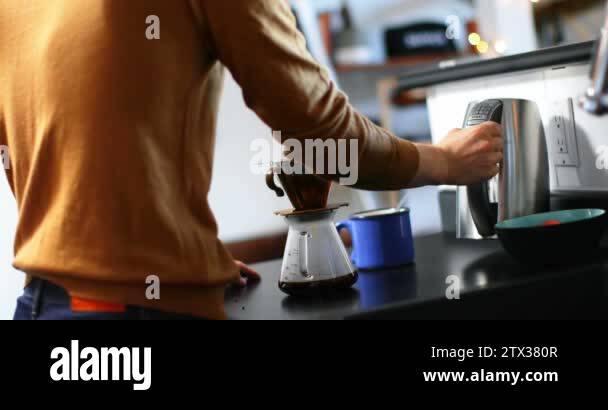 Man pouring beverage from a kettle and pouring into a funnel in kitchen ...