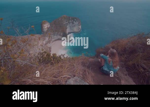 Back view of girl sitting on the cliff and raising hands over beautiful ...