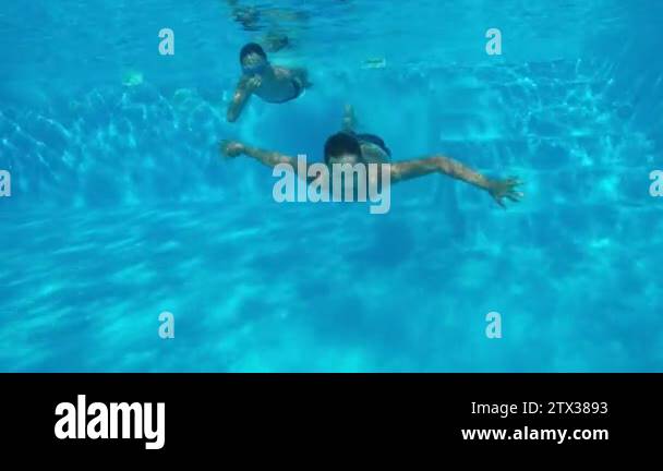 Funny boys swimming underwater in a swimming pool with sky blue water ...