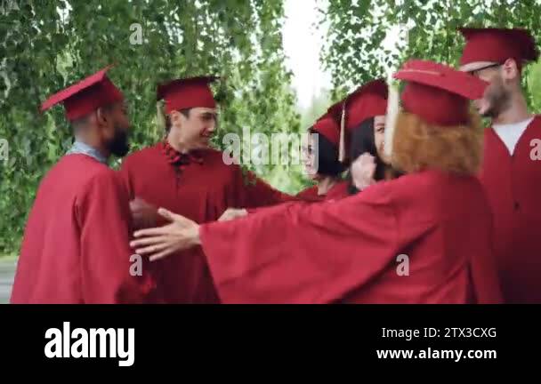 Excited young people graduating students in gowns and hats are hugging ...