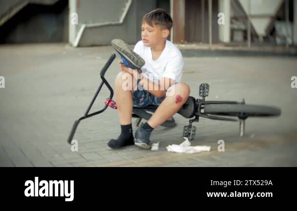 A young boy sits in a park after falling from a bike, calms the pain in ...