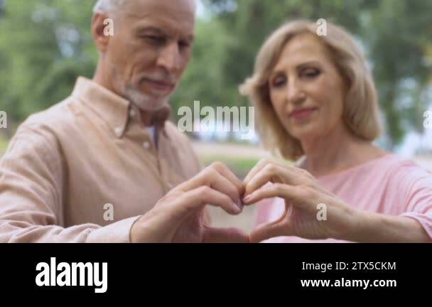 Smiling aged couple showing heart sign, love symbol, happy marriage ...