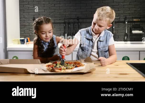Favourite food for kids. Two children slice pizza with pizza cutter ...