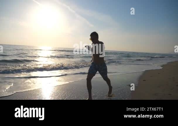 Silhouette of young sporty man running fast along coast during sunrise ...