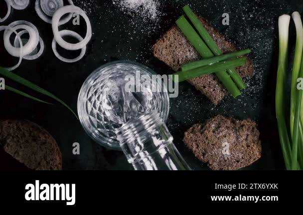 Pour vodka in a glass near the black bread with green onions and salt ...