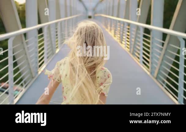 Woman throwing up hair on bridge. Back view of blonde woman running on ...