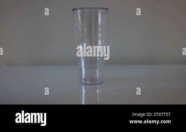 A close-up of a barista hand putting ice cubes into a plastic cup. A ...