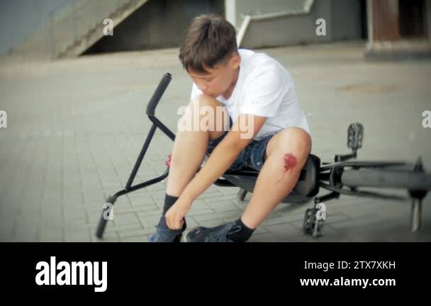 A young boy sits in a park after falling from a bike, calms the pain in ...