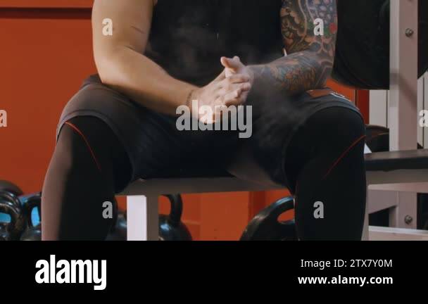 A muscular man with a tattoo covering his hands in talcum and clapping ...