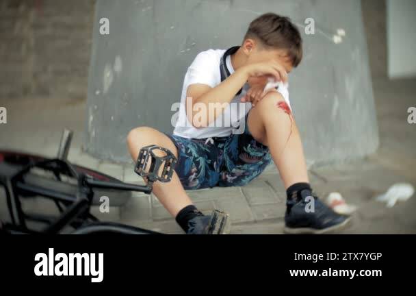 A young boy sits in a park after falling from a bike, calms the pain in ...