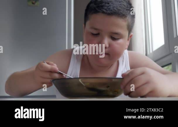 cute little fat boy dining in the kitchen, eating a tablespoon of soup ...