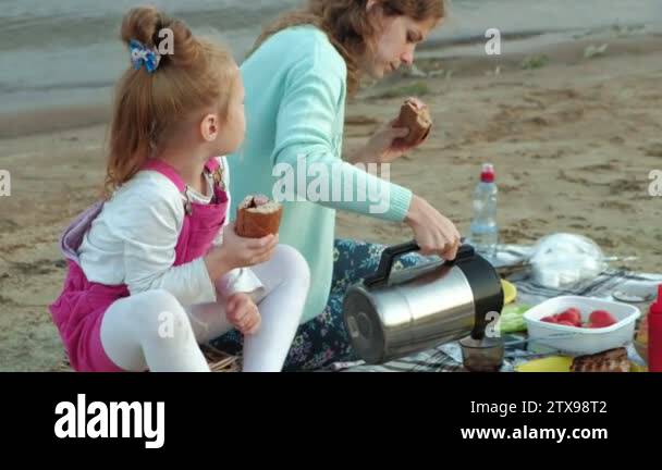 Mother and daughter fry meat and vegetables on a barbecue on the beach ...