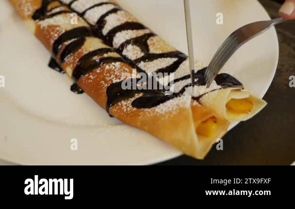 Customer using a fork and knife eat delicious crepes roll with fresh ...