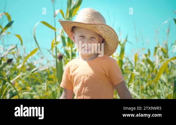 A boy in a straw hat is playing in a cornfield, the child is holding ...