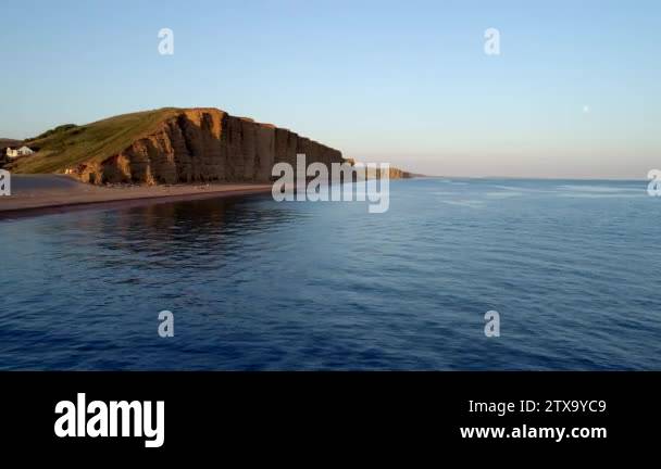 Drone flies very slowly over sea with cliffs of West Bay in Dorset ...